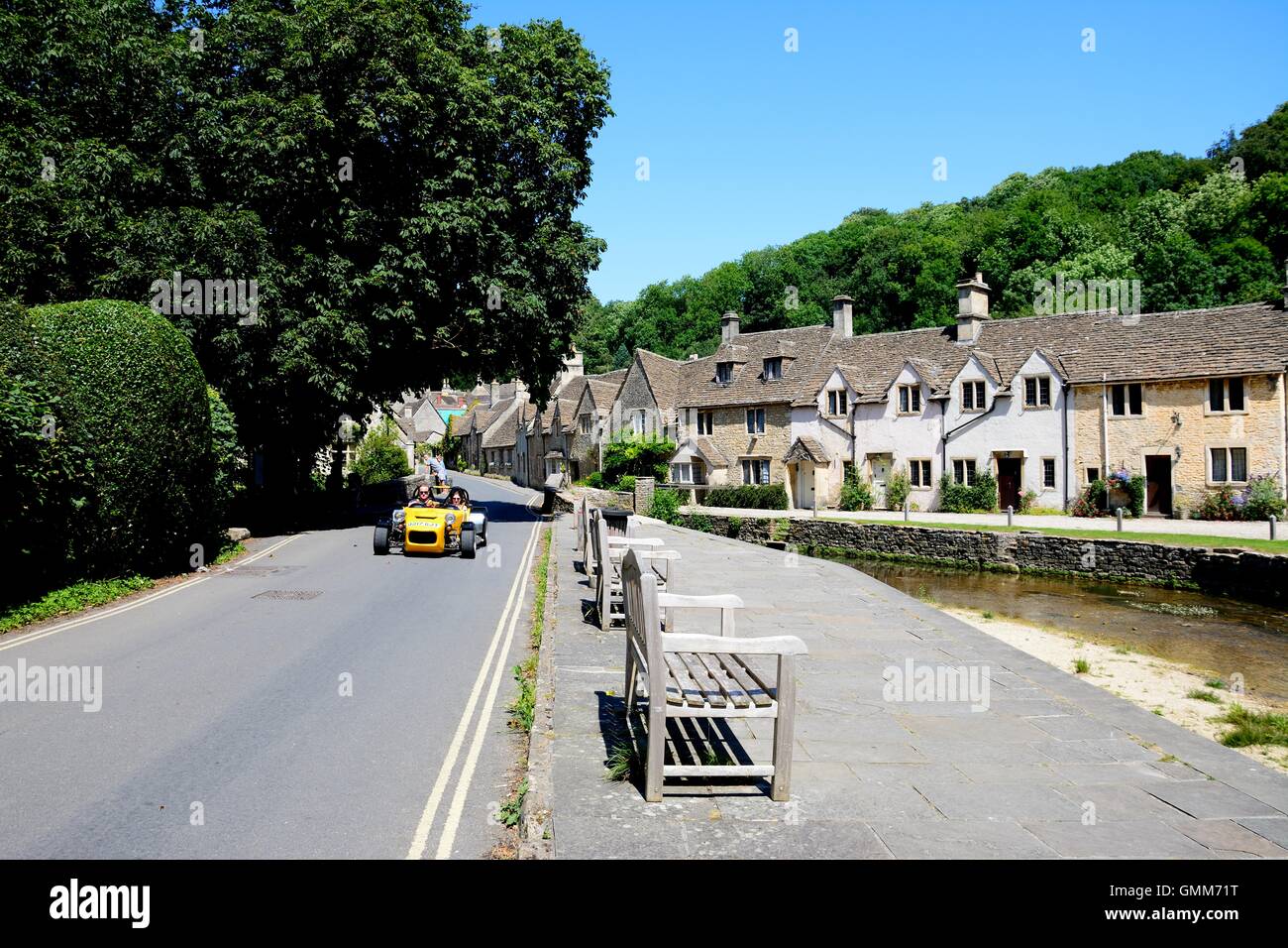 Stone cottages alongside the river Bybrook with wooden benches and a ...