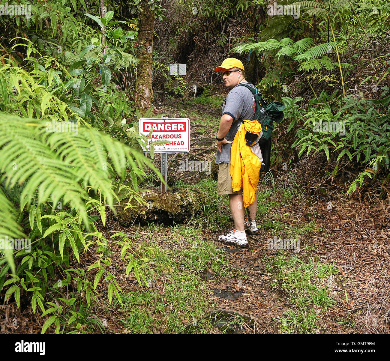 A hiker look over his shoulder while standing in front of a danger sign ...