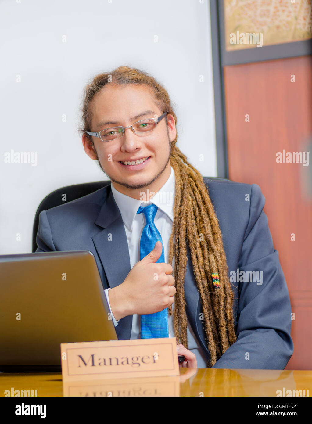 Handsome man with dreads and business suit sitting by desk looking at ...