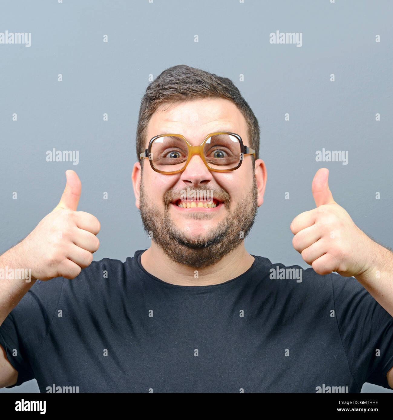 Portrait of a chubby geek showing thumbs up against gray background ...