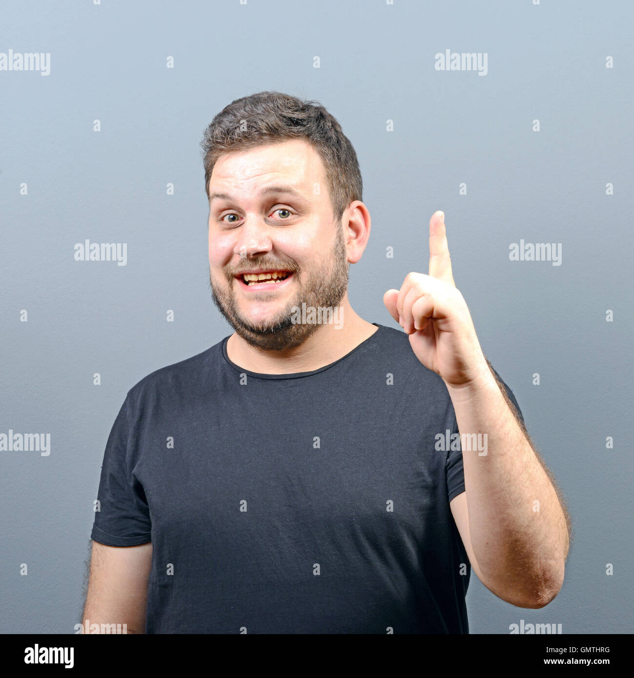 Portrait of man pointing up as a sign of having an idea against gray ...