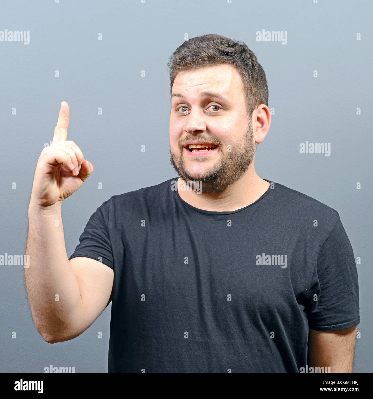 Portrait of man pointing up as a sign of having an idea against gray ...