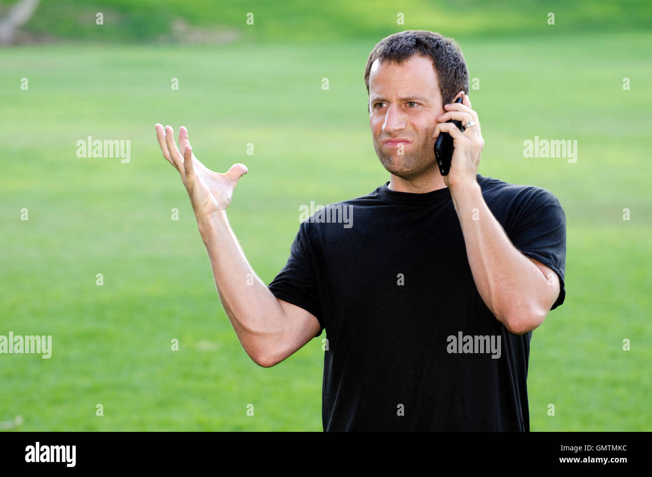 Frustrated angry man on his cell phone outdoors in a black t-shirt ...