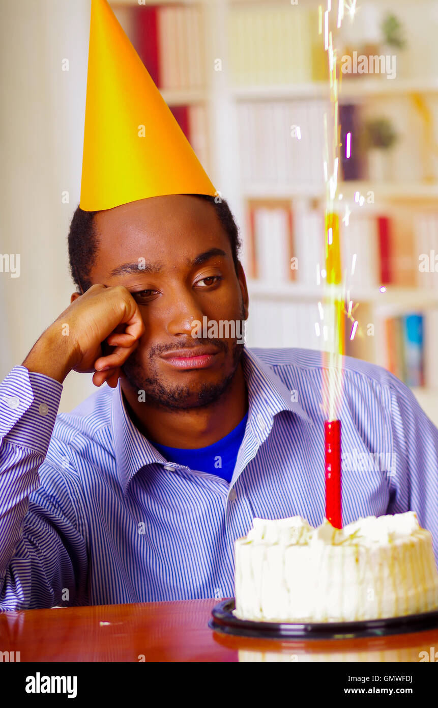 Sad man wearing blue shirt and hat sitting by table with cake in front ...