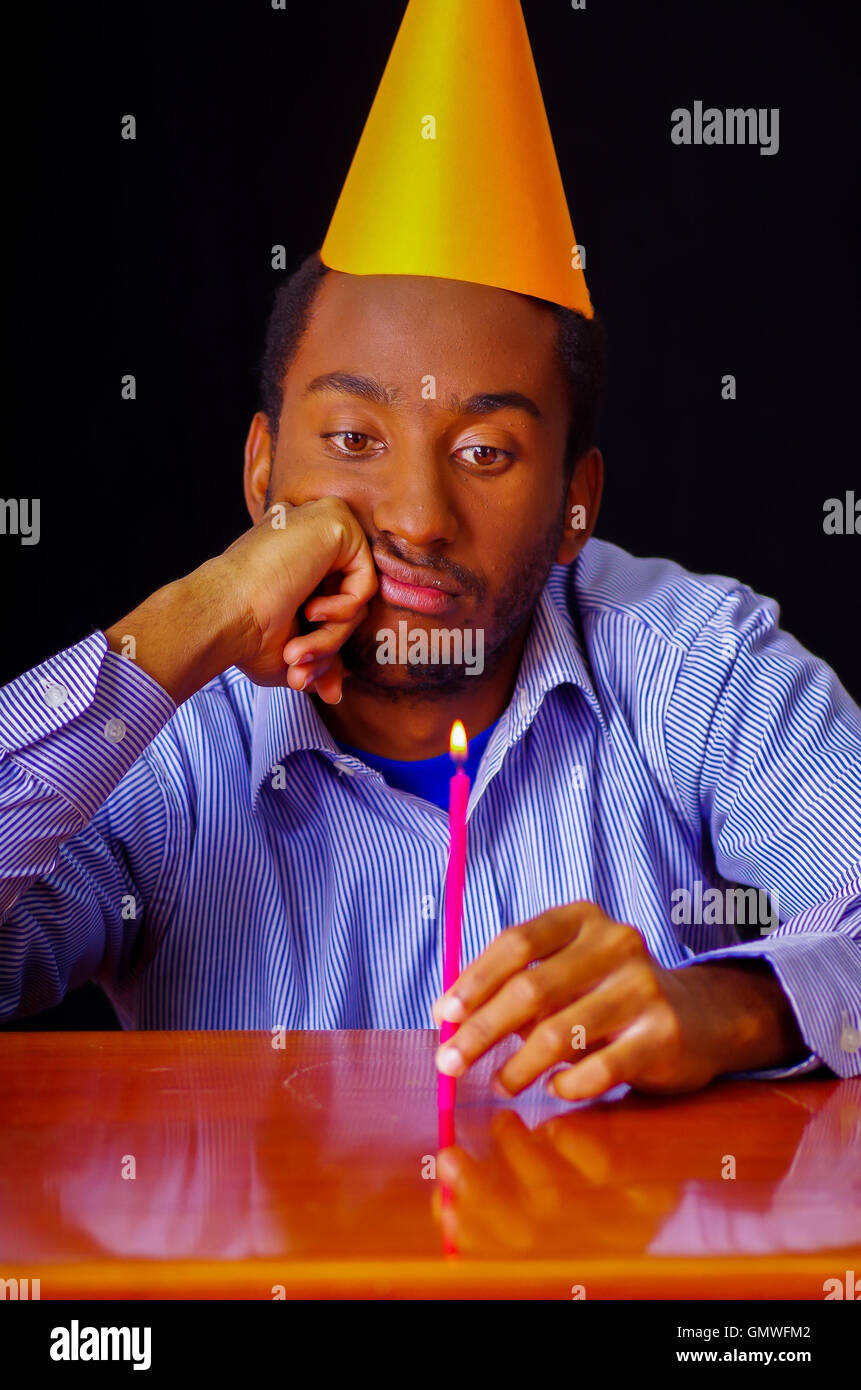 Bored looking man wearing blue shirt and hat sitting by table holding a ...
