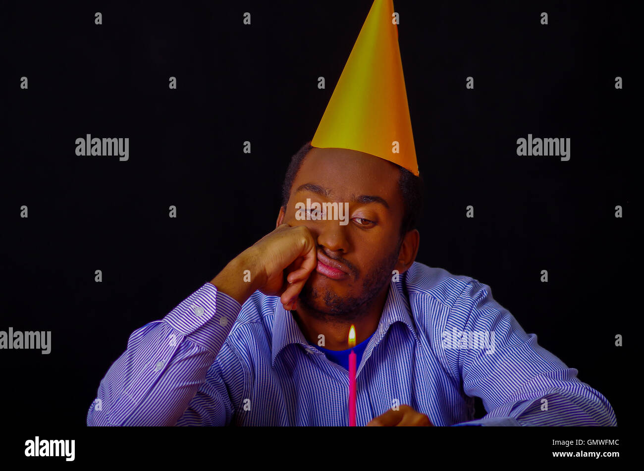 Bored looking man wearing blue shirt and hat sitting by table holding a ...
