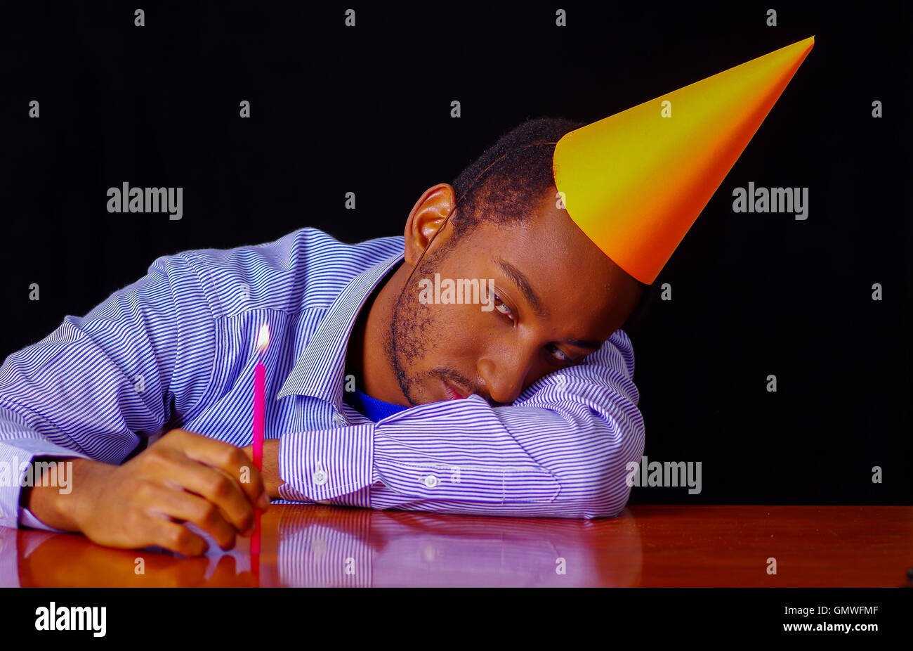 Bored looking man wearing blue shirt and hat sitting by table holding a ...