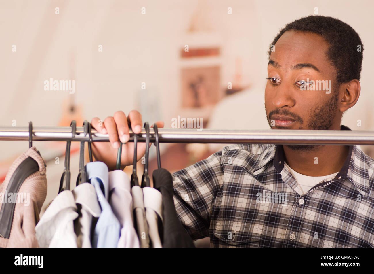 Handsome young man standing inside wardrobe going through rack of ...