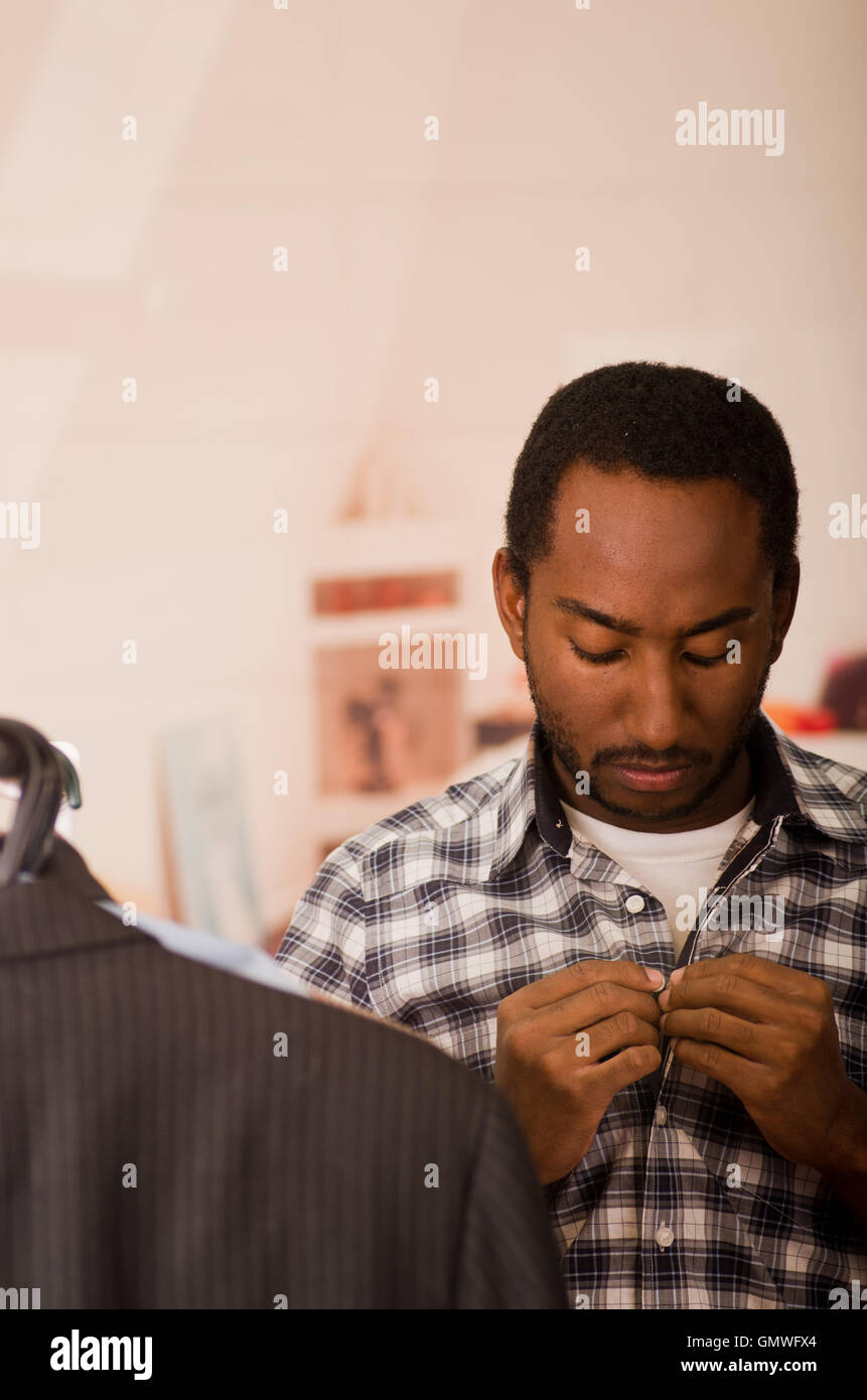 Handsome young man putting on square pattern shirt, buttoning up facing ...