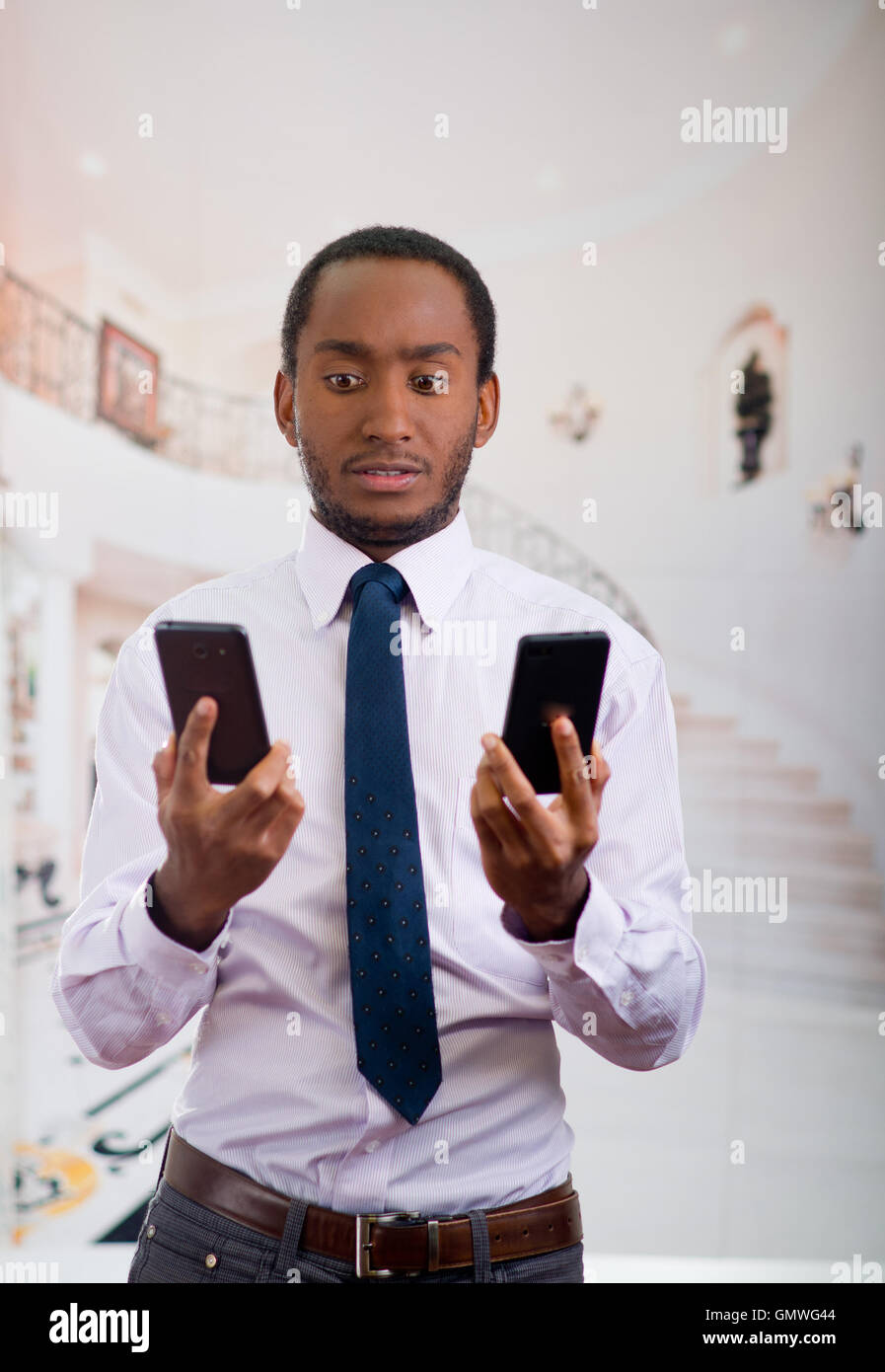 Handsome Man Wearing Shirt And Tie Holding Up Two Mobile Phones With