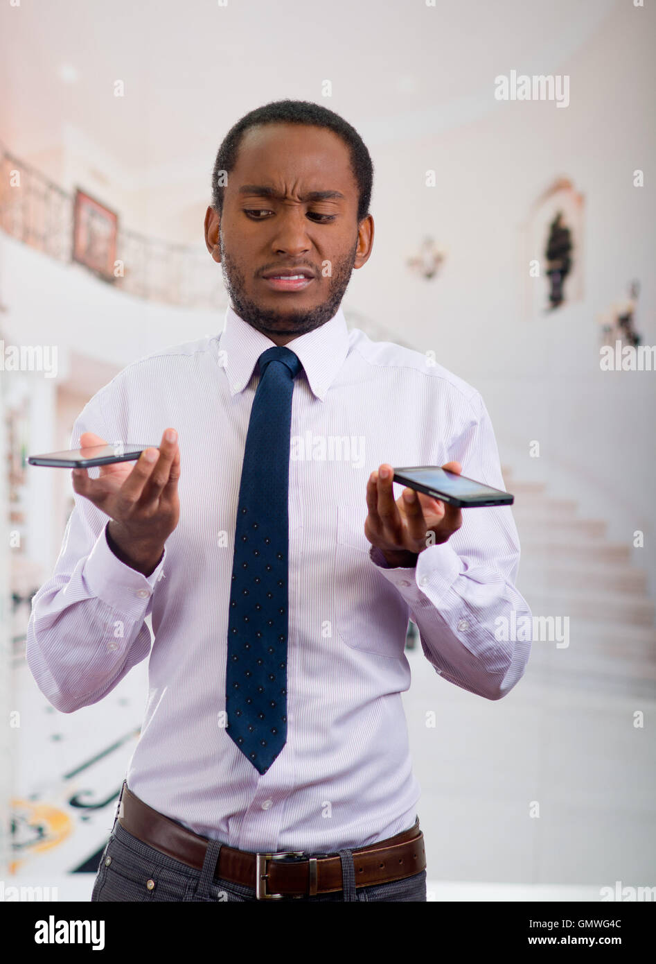 Handsome Man Wearing Shirt And Tie Holding Up Two Mobile Phones With