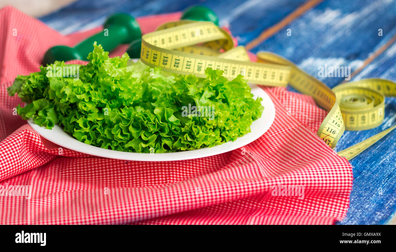 Fitness composition of green lettuce on white plate, weights and ruler ...