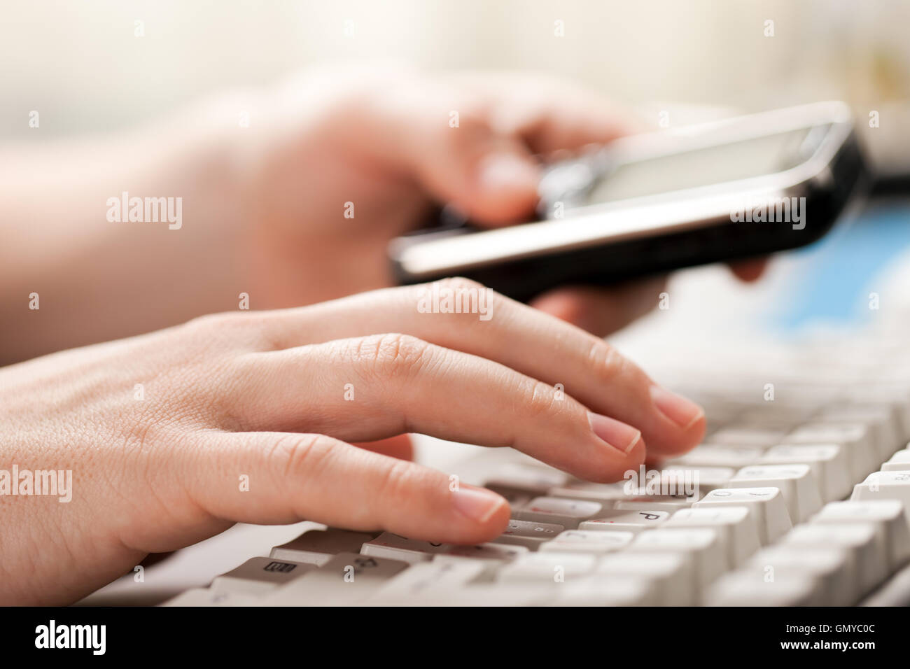 Holding phone hand typing computer keyboard Stock Photo - Alamy