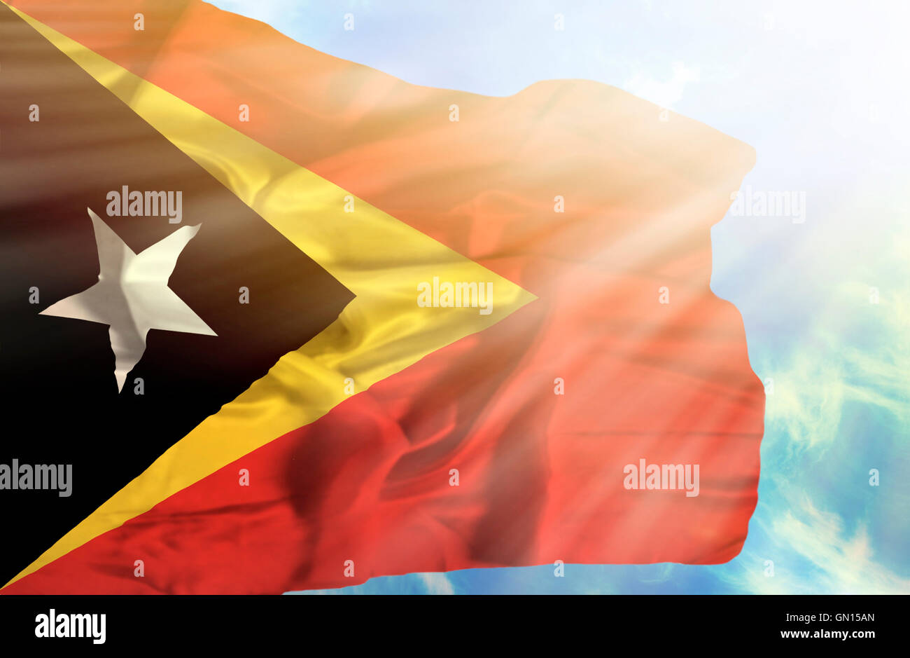East Timor waving flag against blue sky with sunrays Stock Photo - Alamy