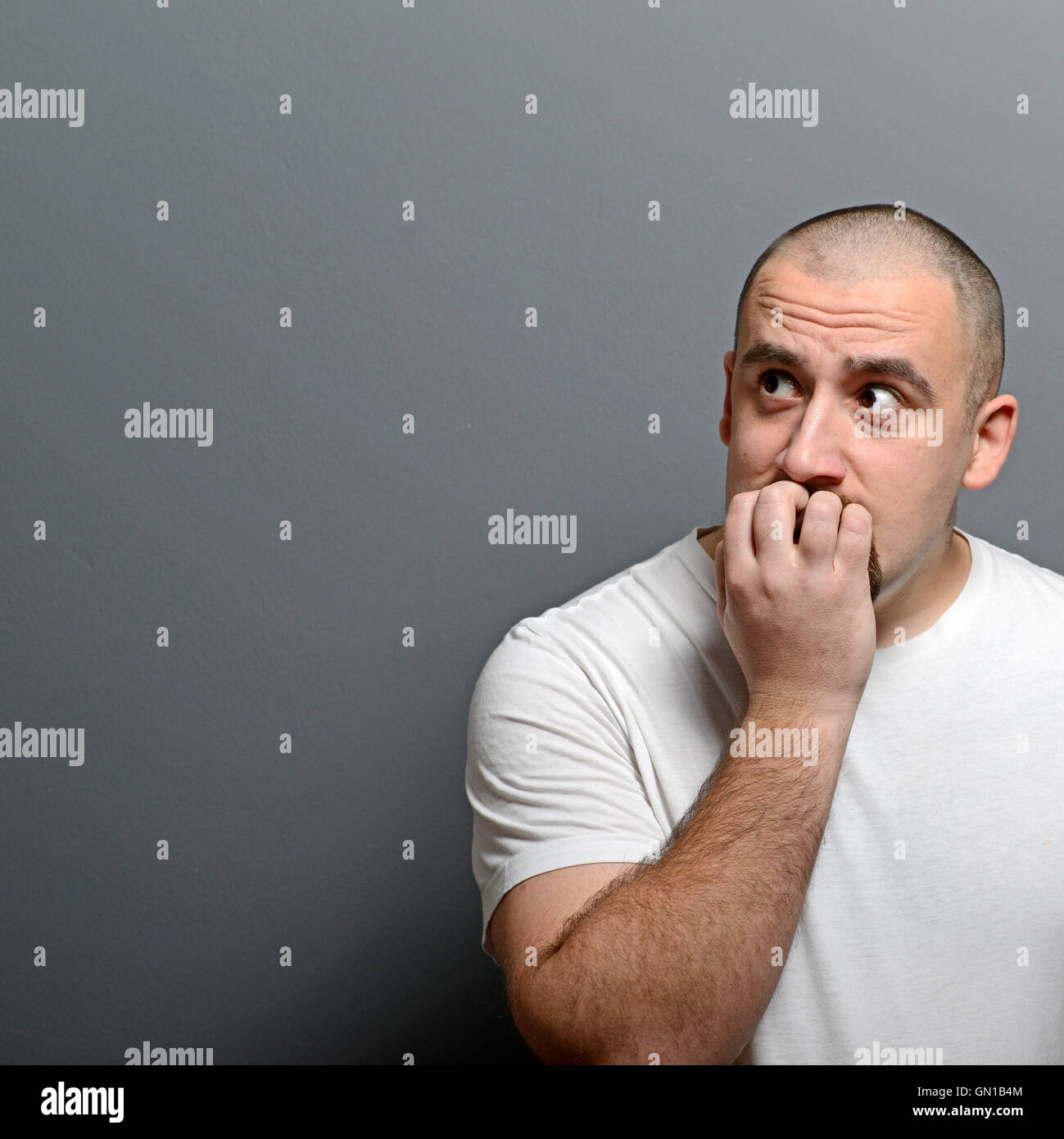 Portrait of a man biting nails and being scared against gray background ...