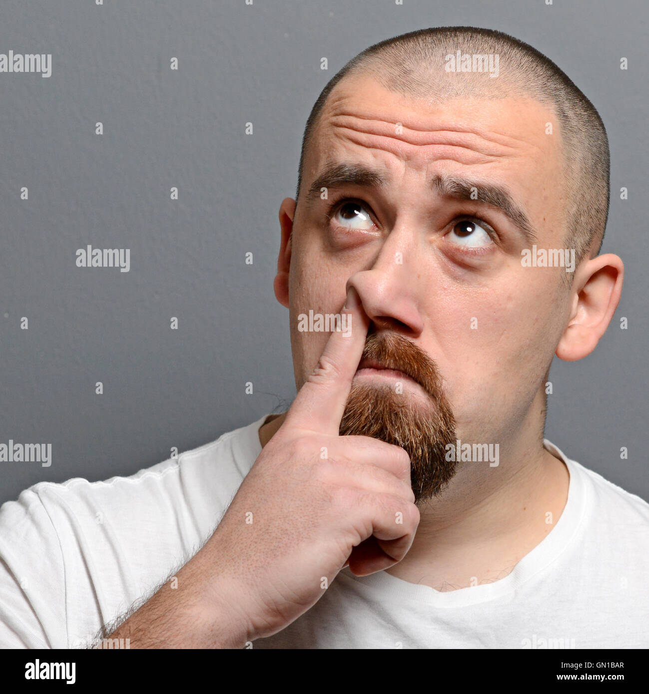 Portrait of a man putting finger in his nose against gray background ...