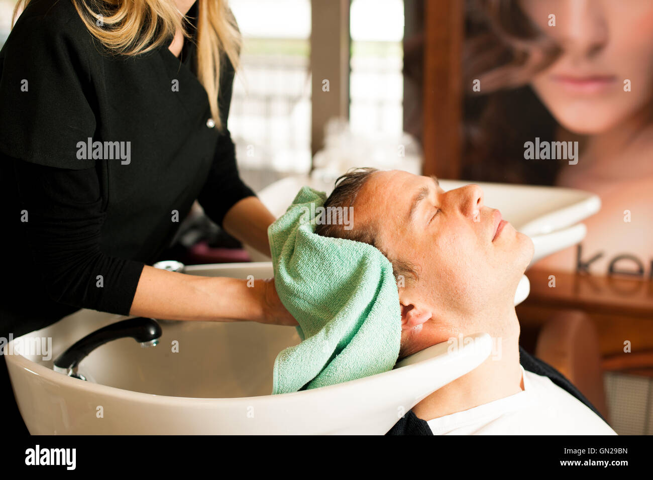 Female hairdresser washing hair of smiling man client at beauty parlour ...