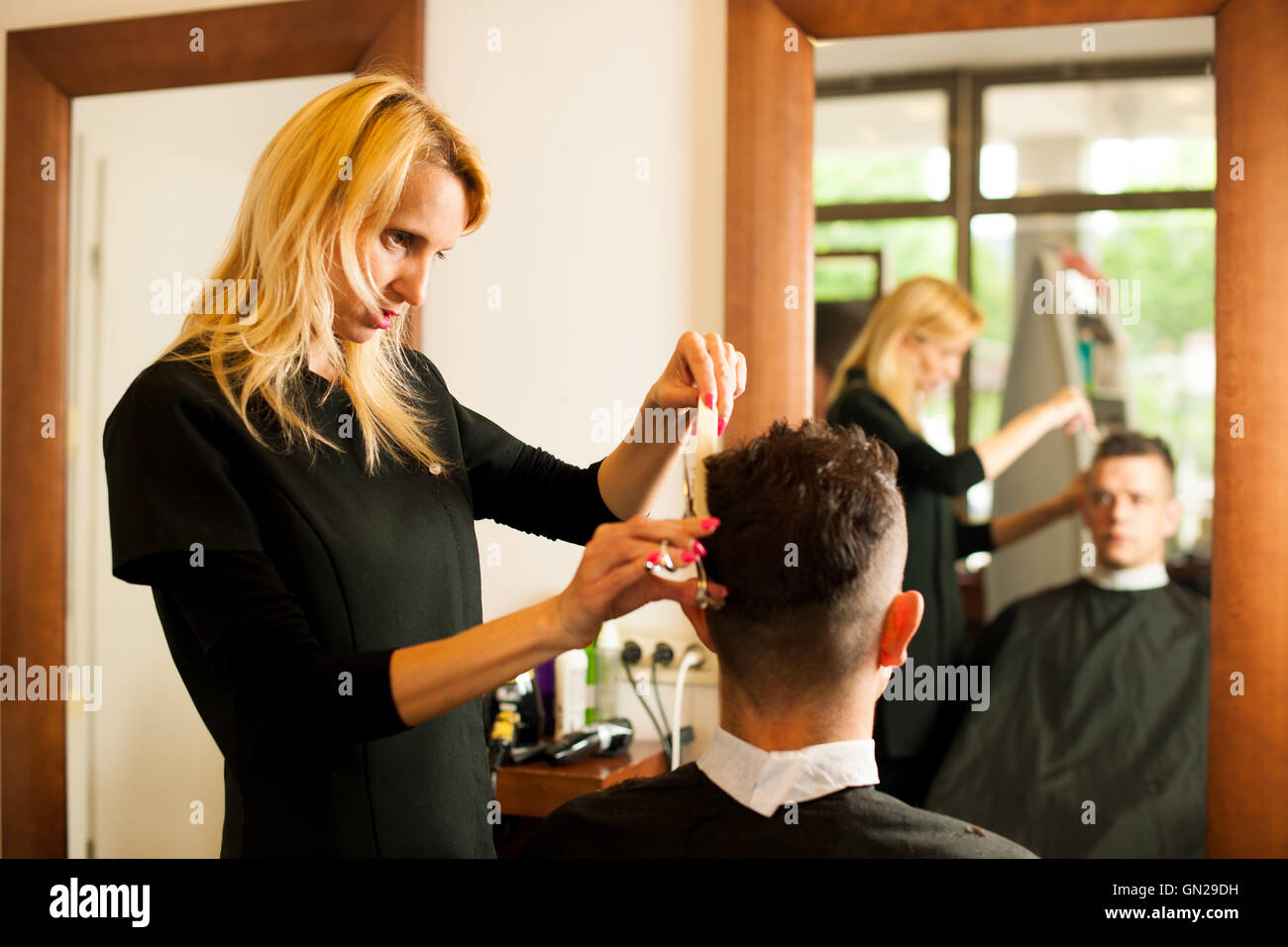 Female hairdresser cutting hair of smiling man client at beauty parlour ...