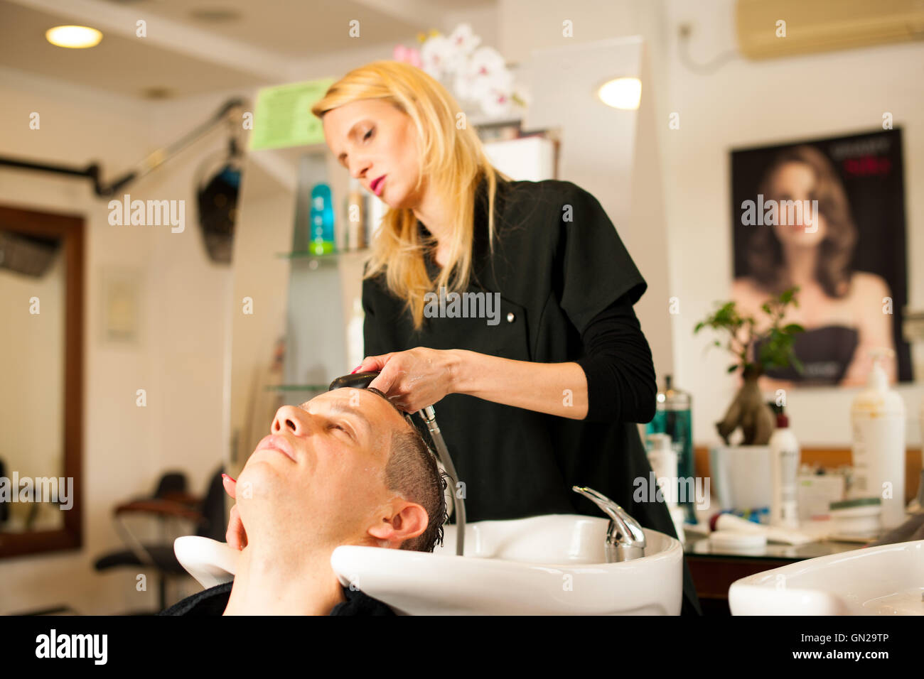 Female hairdresser washing hair of smiling man client at beauty parlour ...