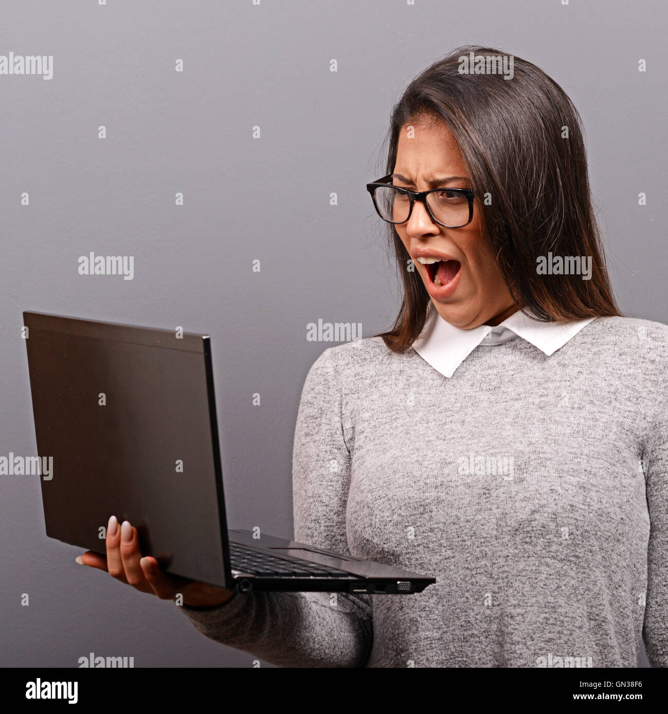 Portrait of angry woman screaming at her laptop against gray background ...