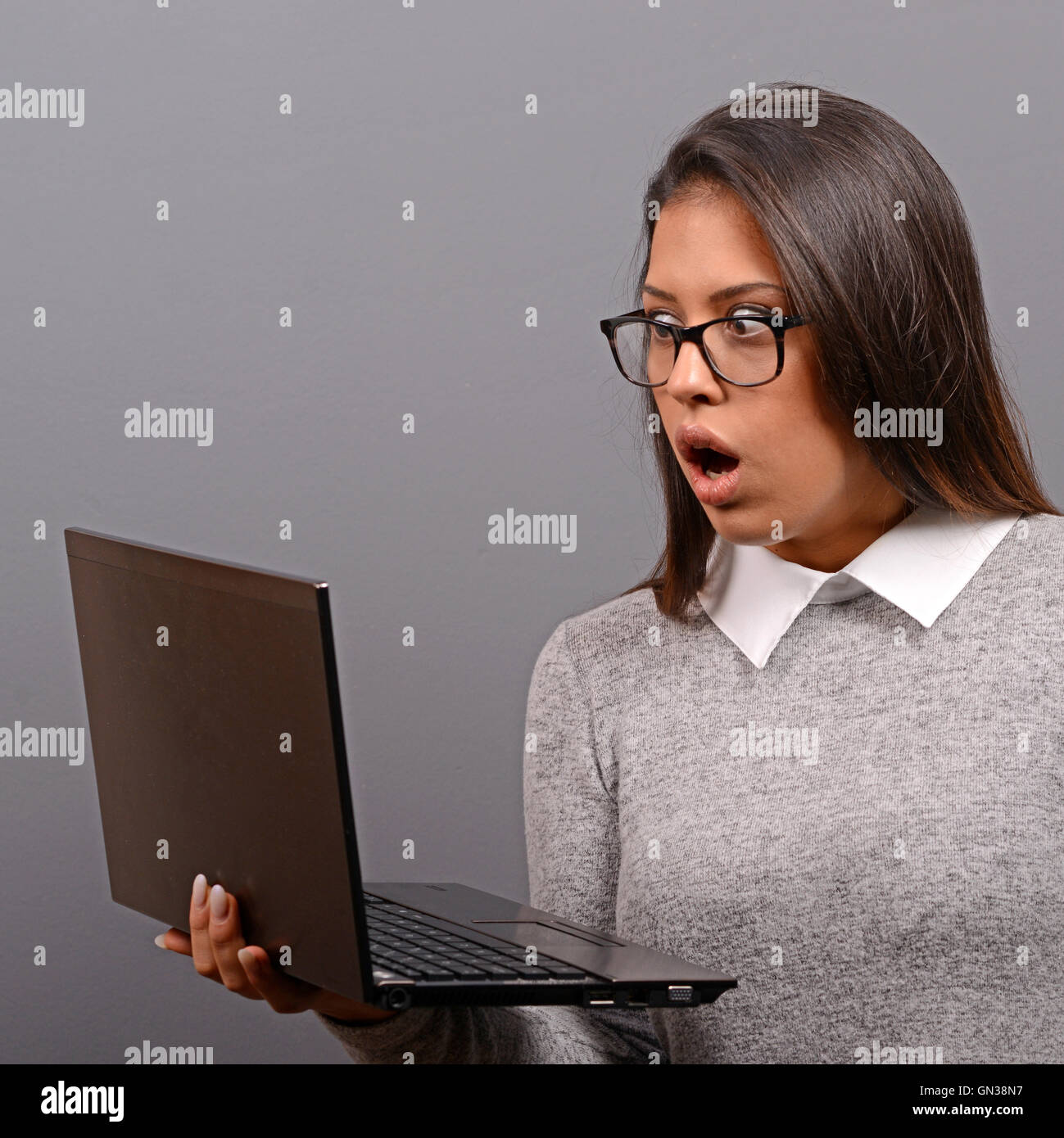 Portrait of woman in shock what she sees at her laptop against gray ...