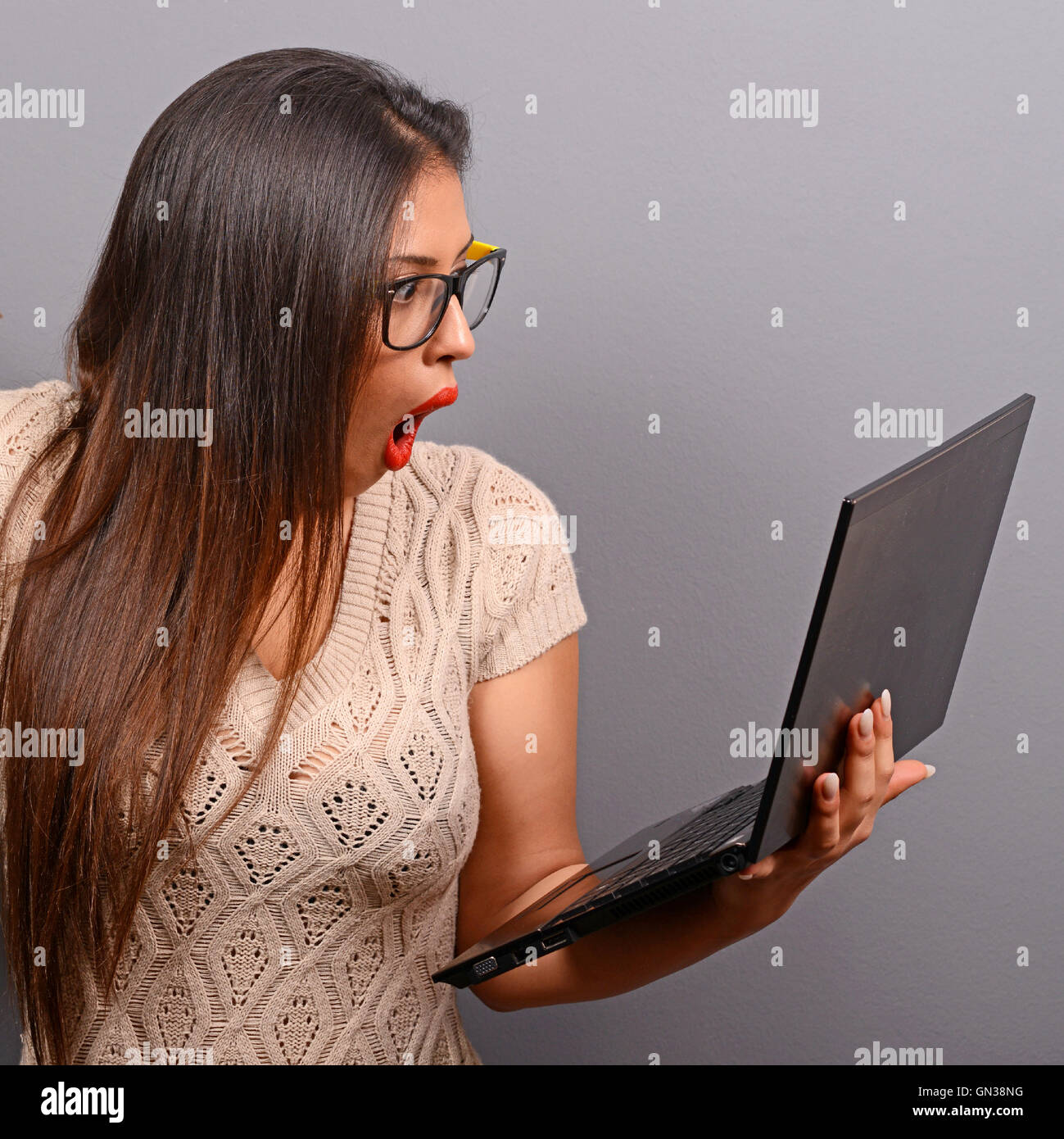 Portrait of woman in shock what she sees at her laptop against gray ...