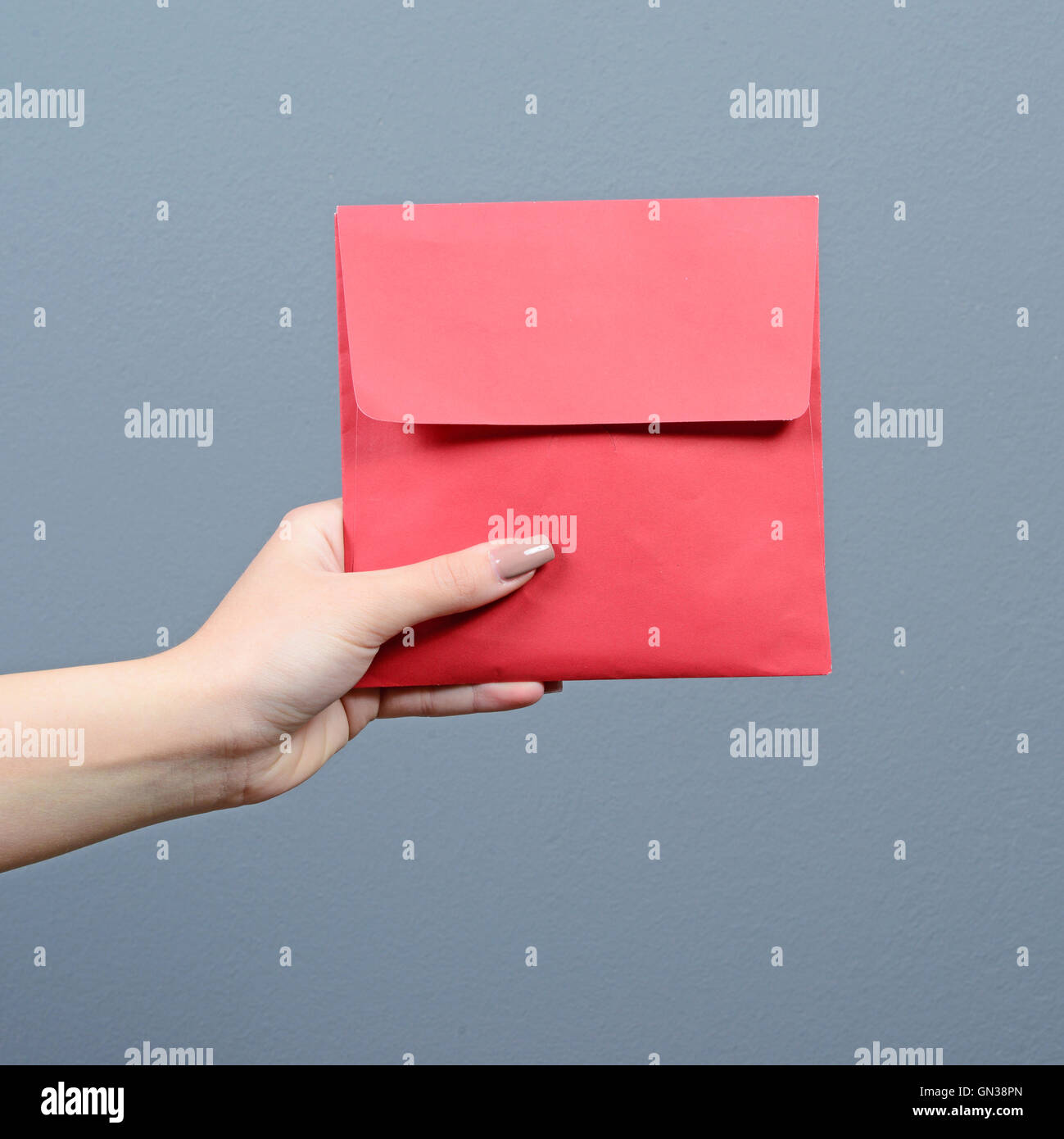 Hand holding red envelope against gray background Stock Photo - Alamy