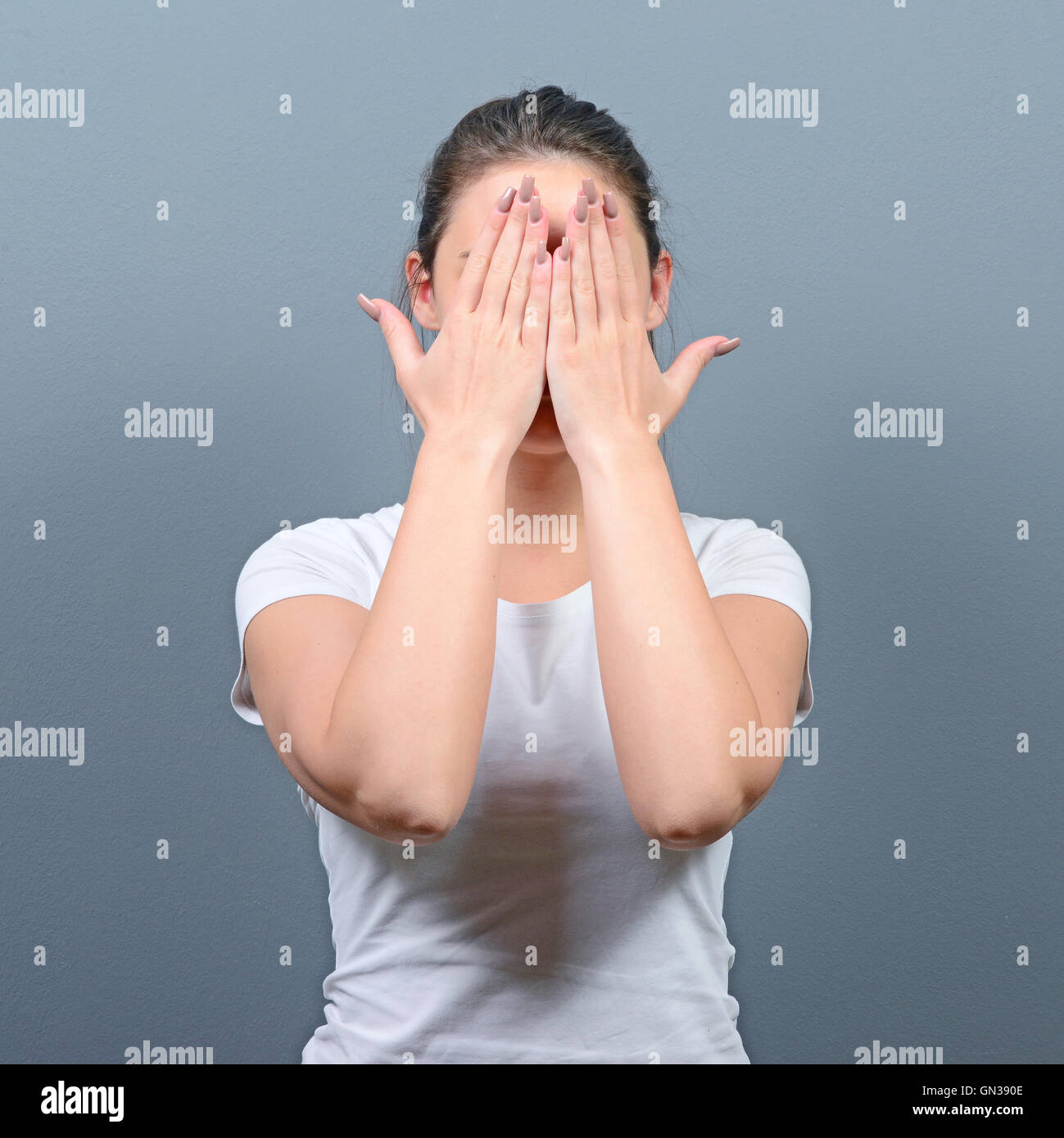 Portrait of woman hiding her face with both hands against gray ...
