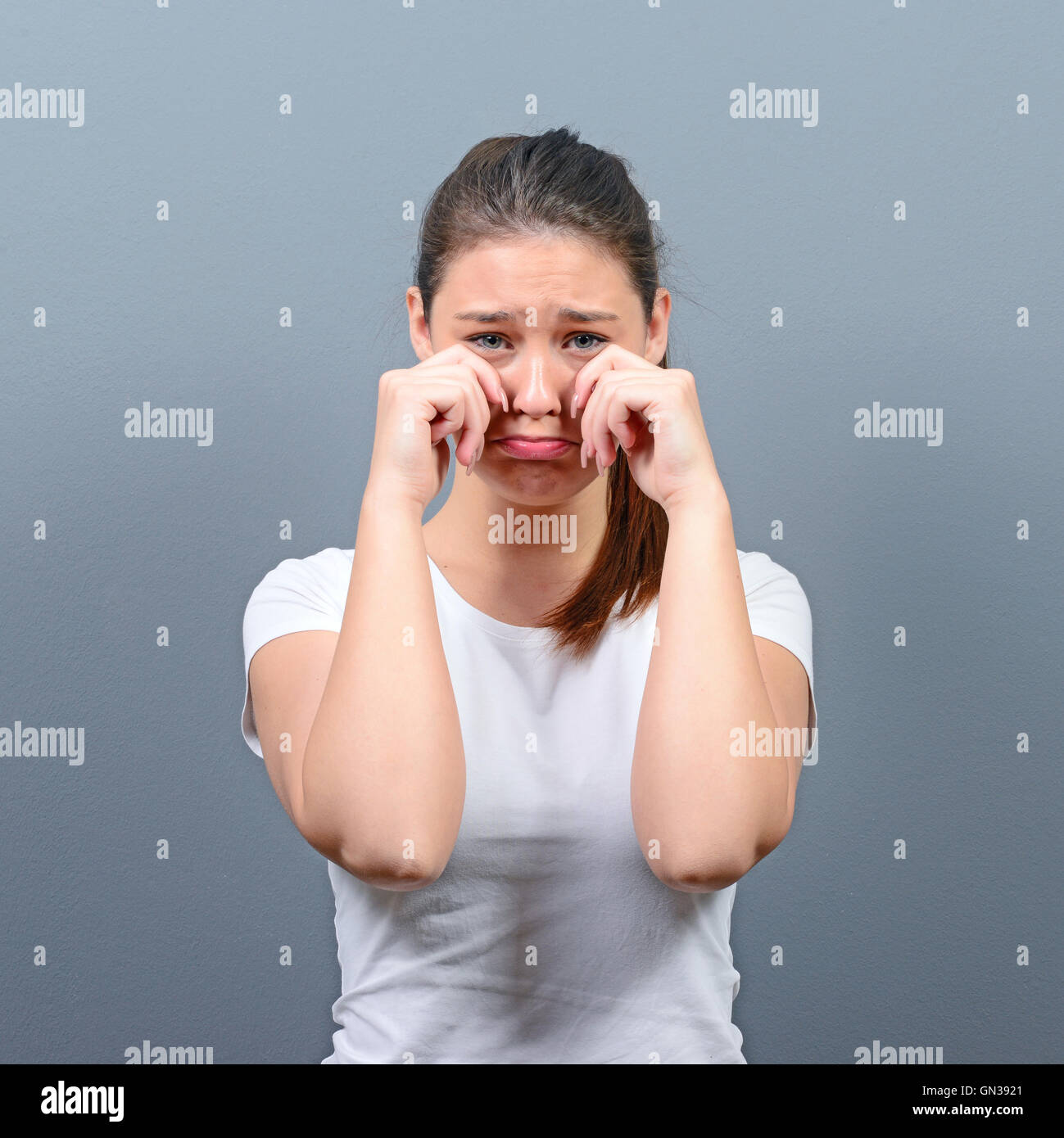 Woman crying and wiping tears against gray background Stock Photo - Alamy
