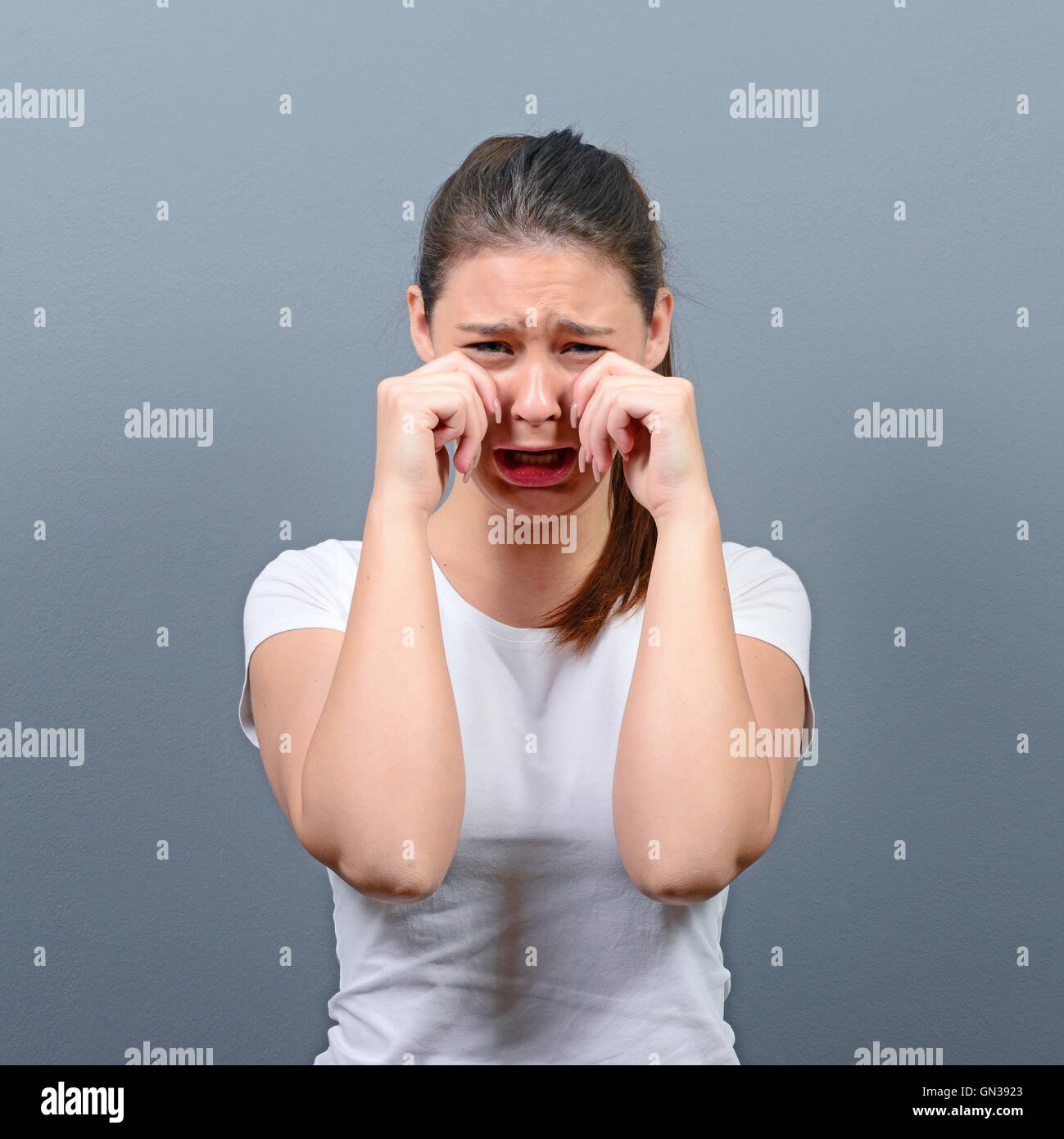 Woman crying and wiping tears against gray background Stock Photo - Alamy