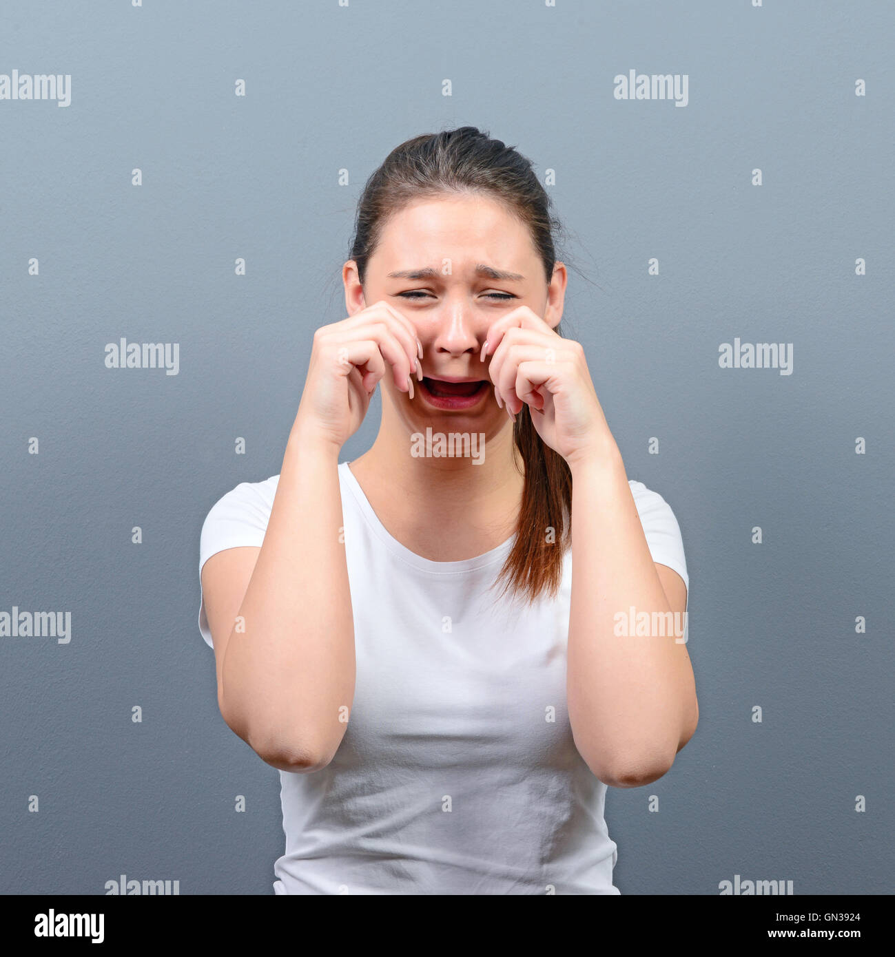 Woman crying and wiping tears against gray background Stock Photo - Alamy