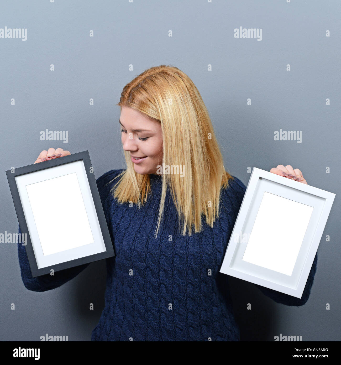Portrait of smiling woman holding blank photo frames against gray ...