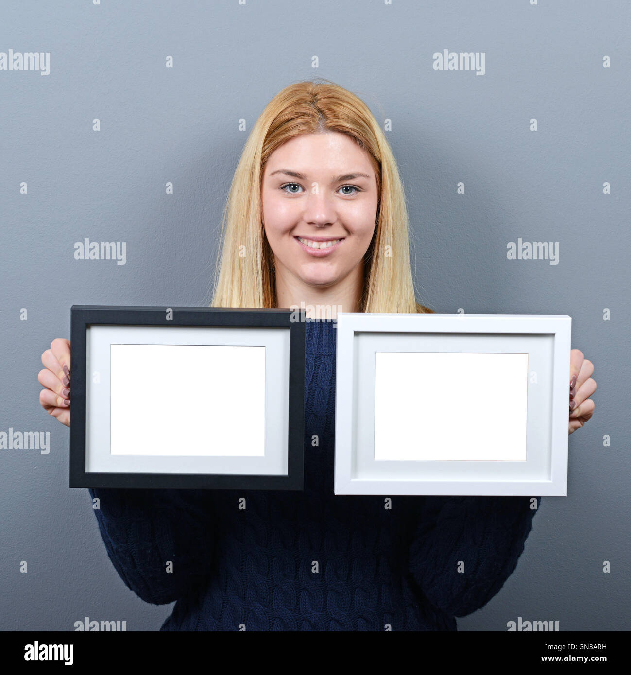 Portrait of smiling woman holding blank photo frames against gray ...