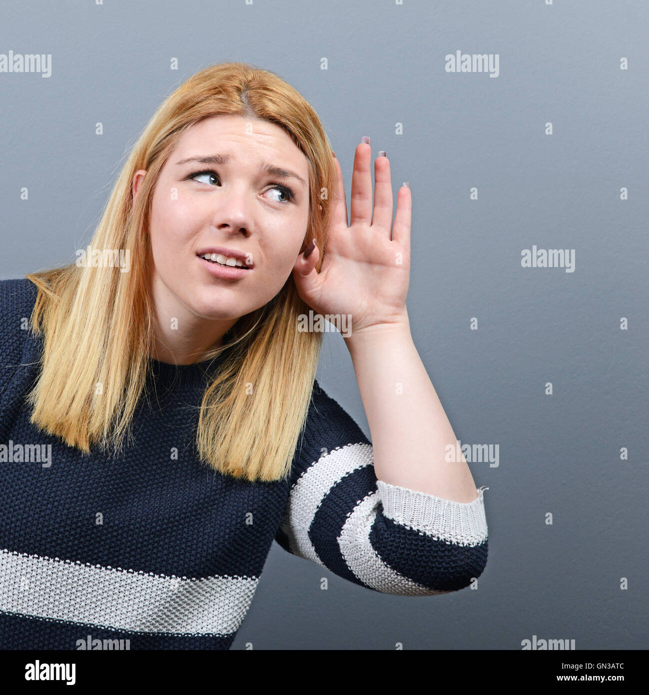 Portrait of woman trying to listen something against gray background ...