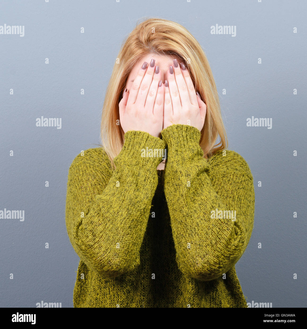 Portrait of woman hiding her face with both hands against gray ...