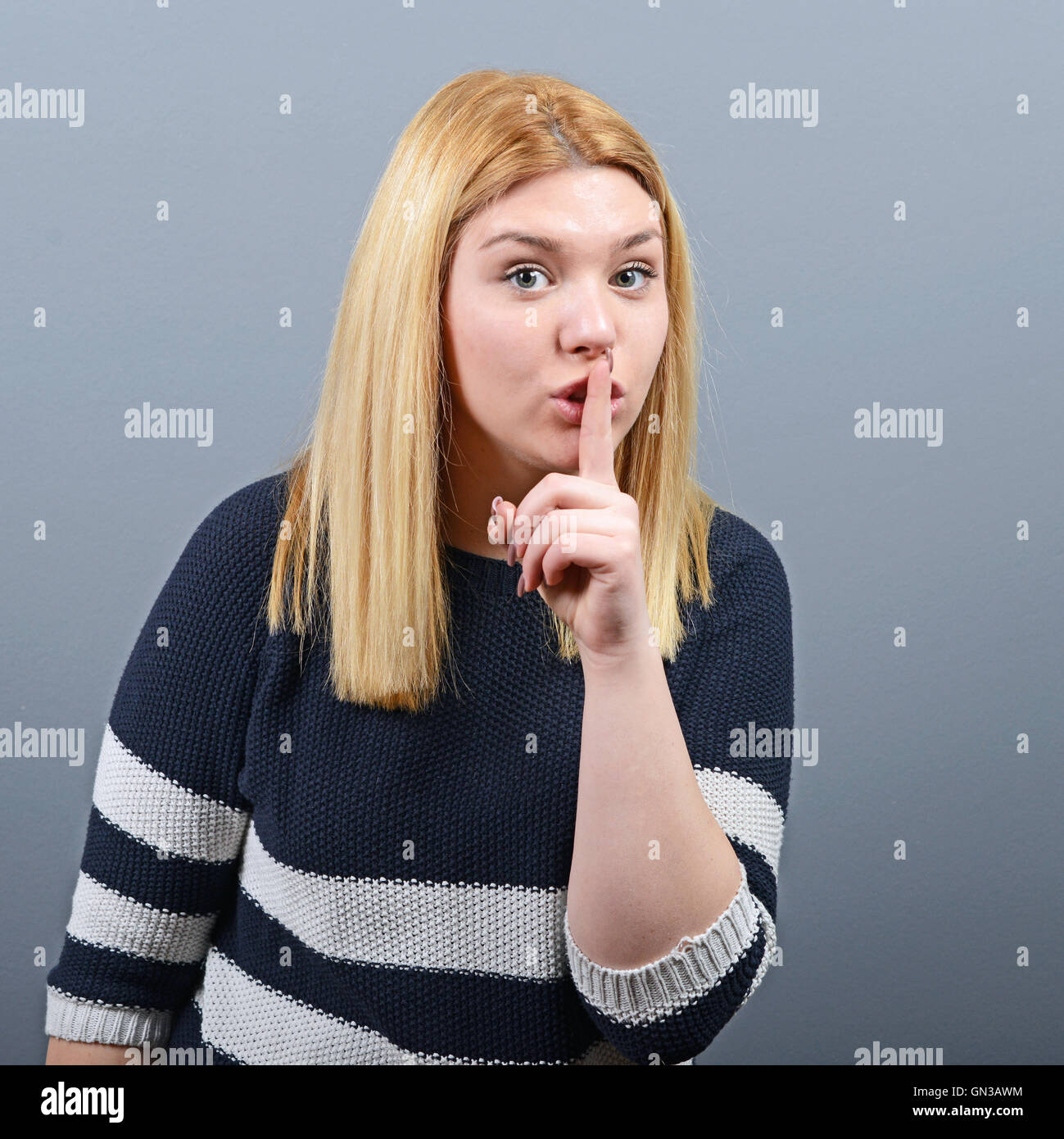 Portrait of woman holding finger over lips as silent gesture against ...