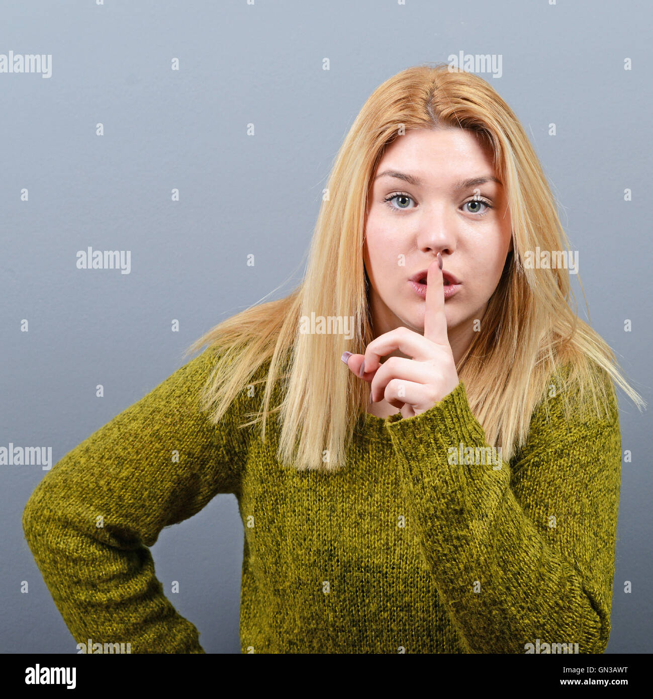 Portrait of woman holding finger over lips as silent gesture against ...