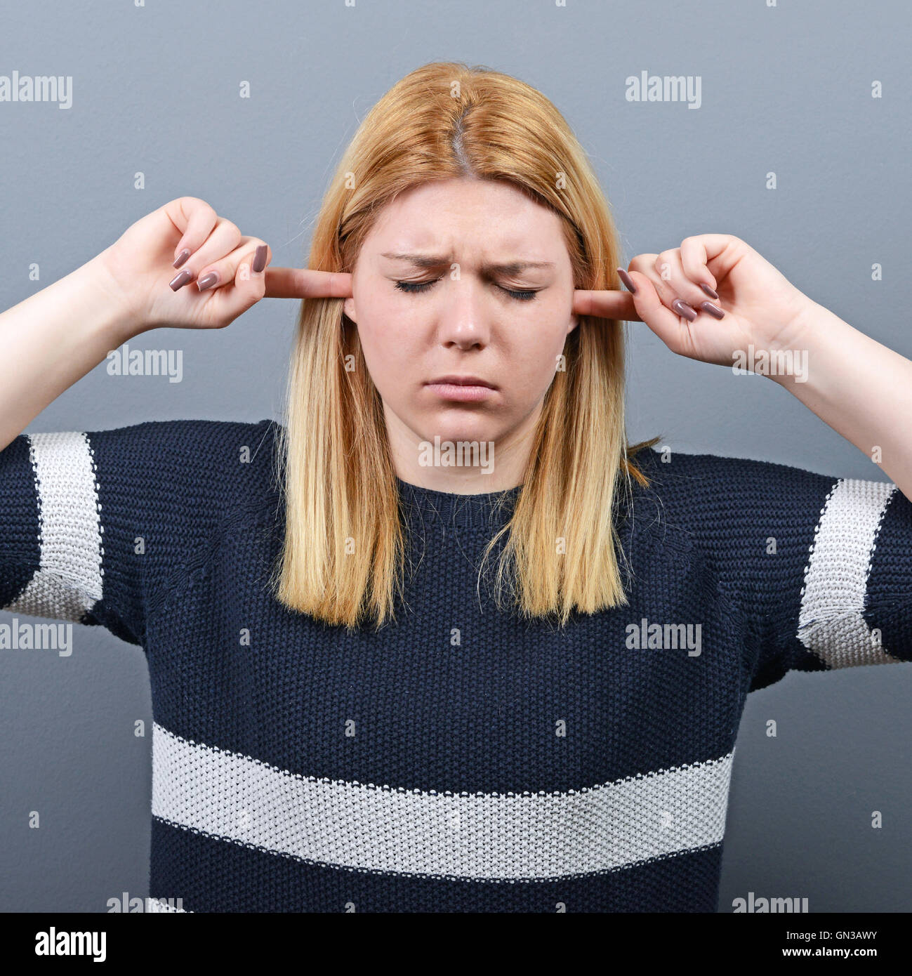 Portrait of woman pluging ears against gray background Stock Photo - Alamy