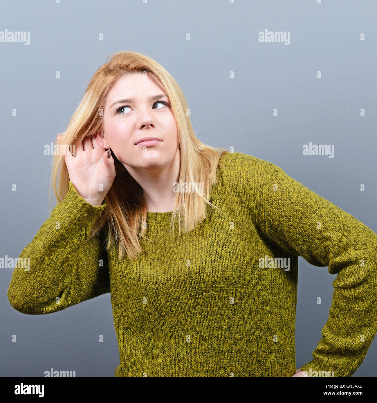Portrait of woman trying to listen something against gray background ...