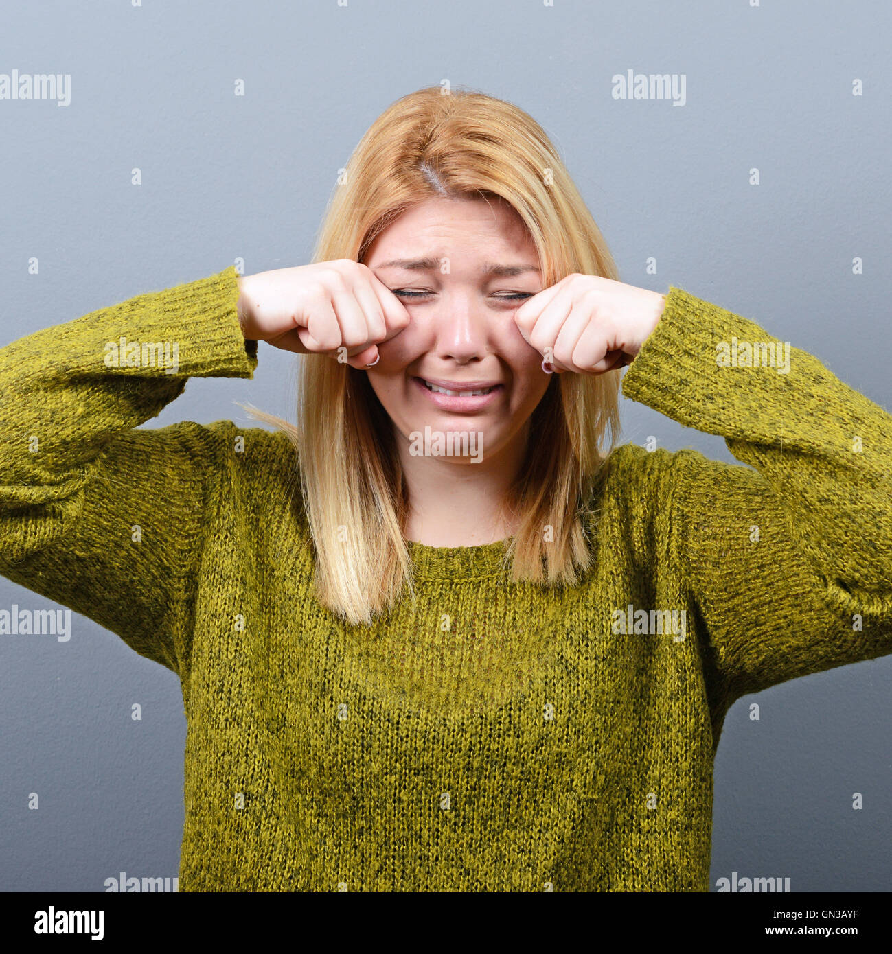 Woman crying and wiping tears against gray background Stock Photo - Alamy