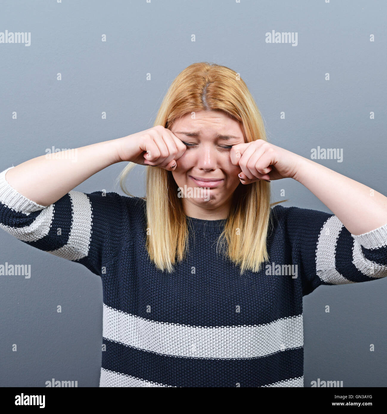 Woman crying and wiping tears against gray background Stock Photo - Alamy