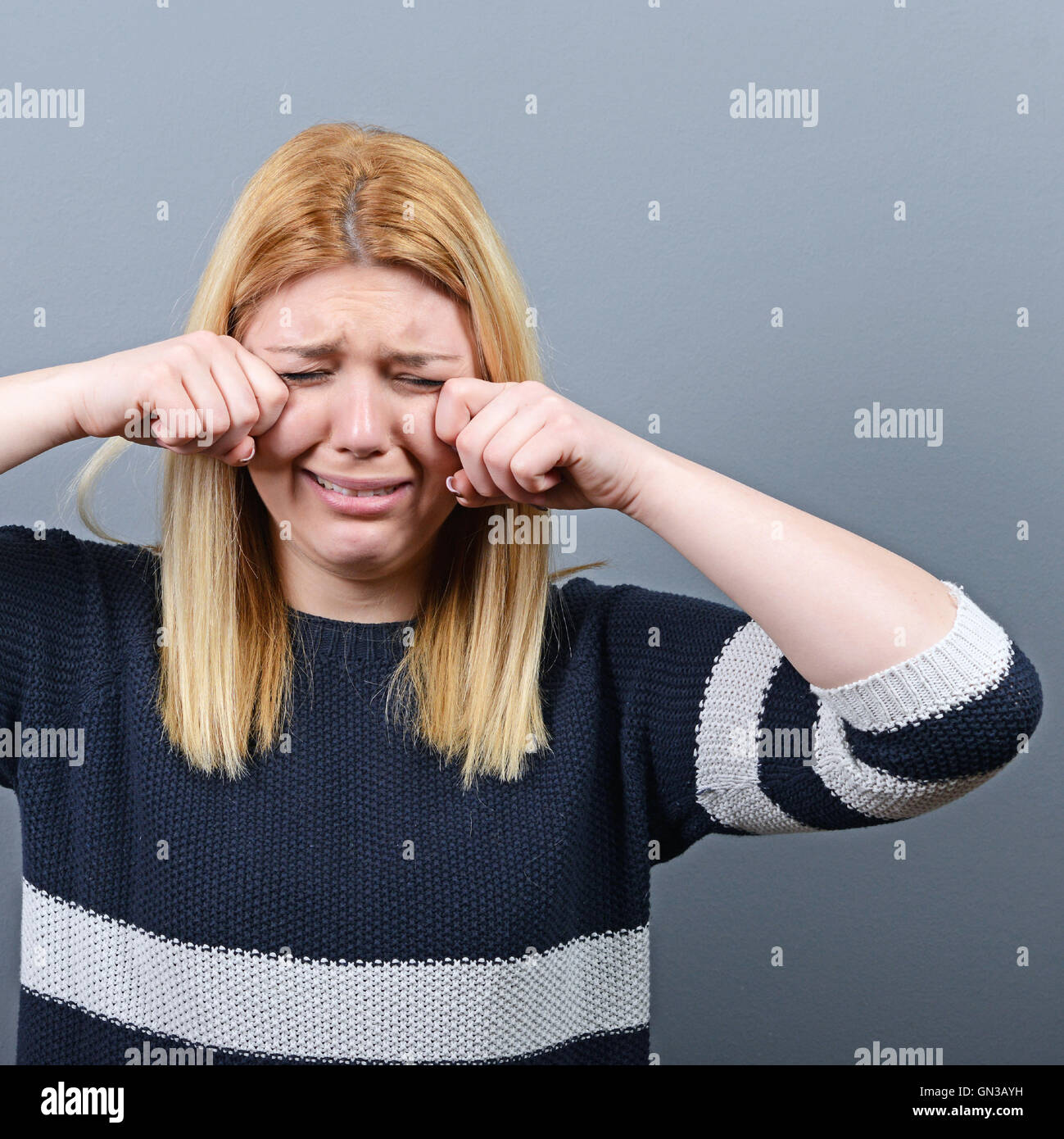 Woman crying and wiping tears against gray background Stock Photo - Alamy