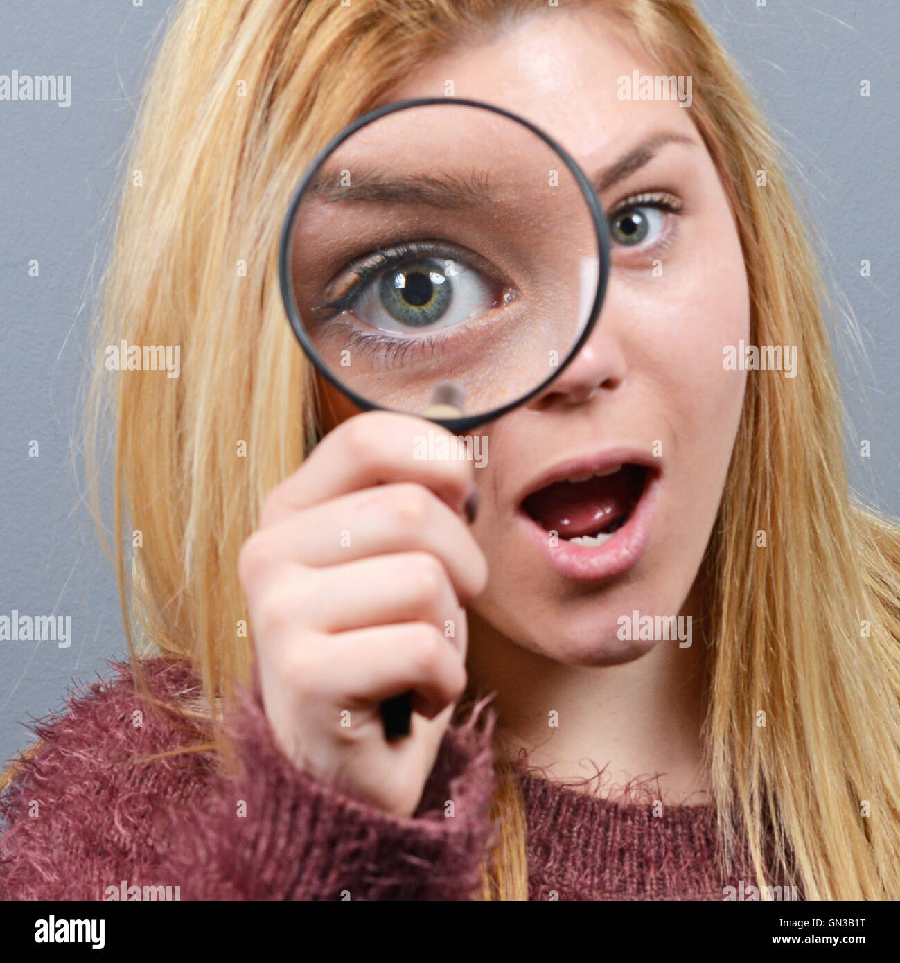 Woman with magnifying glass against gray background Stock Photo - Alamy