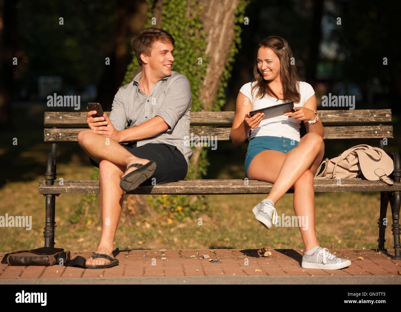 Young couple having fun on a bench in park while socializing over web ...