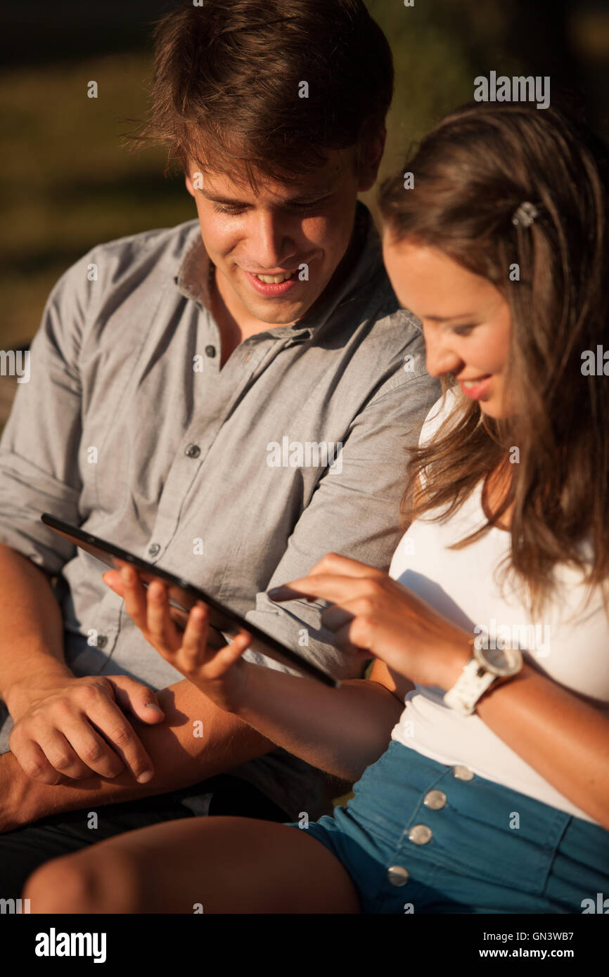 Young couple having fun on a bench in park while socializing over web ...