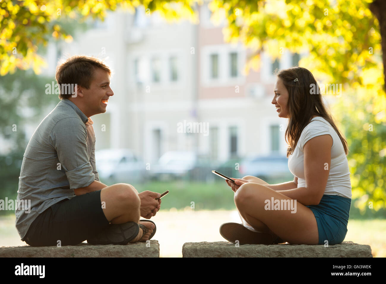 Young couple having fun on a bench in park while socializing over web ...