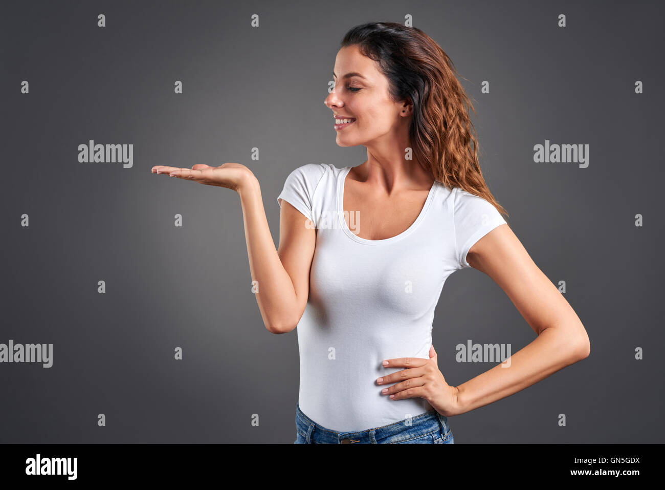A beautiful young woman smiling and showing sideways with her hand ...