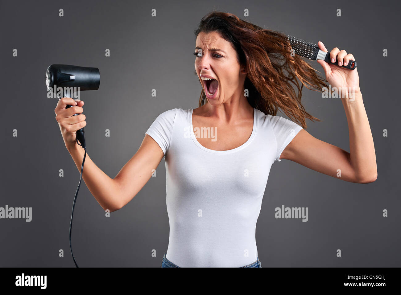 A beautiful young woman screaming while using a hairdryer and a ...