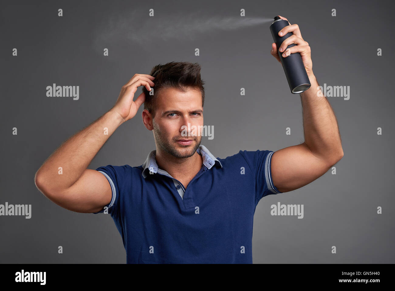 A handsome young man smiling while fixing his hair with a hairspray ...