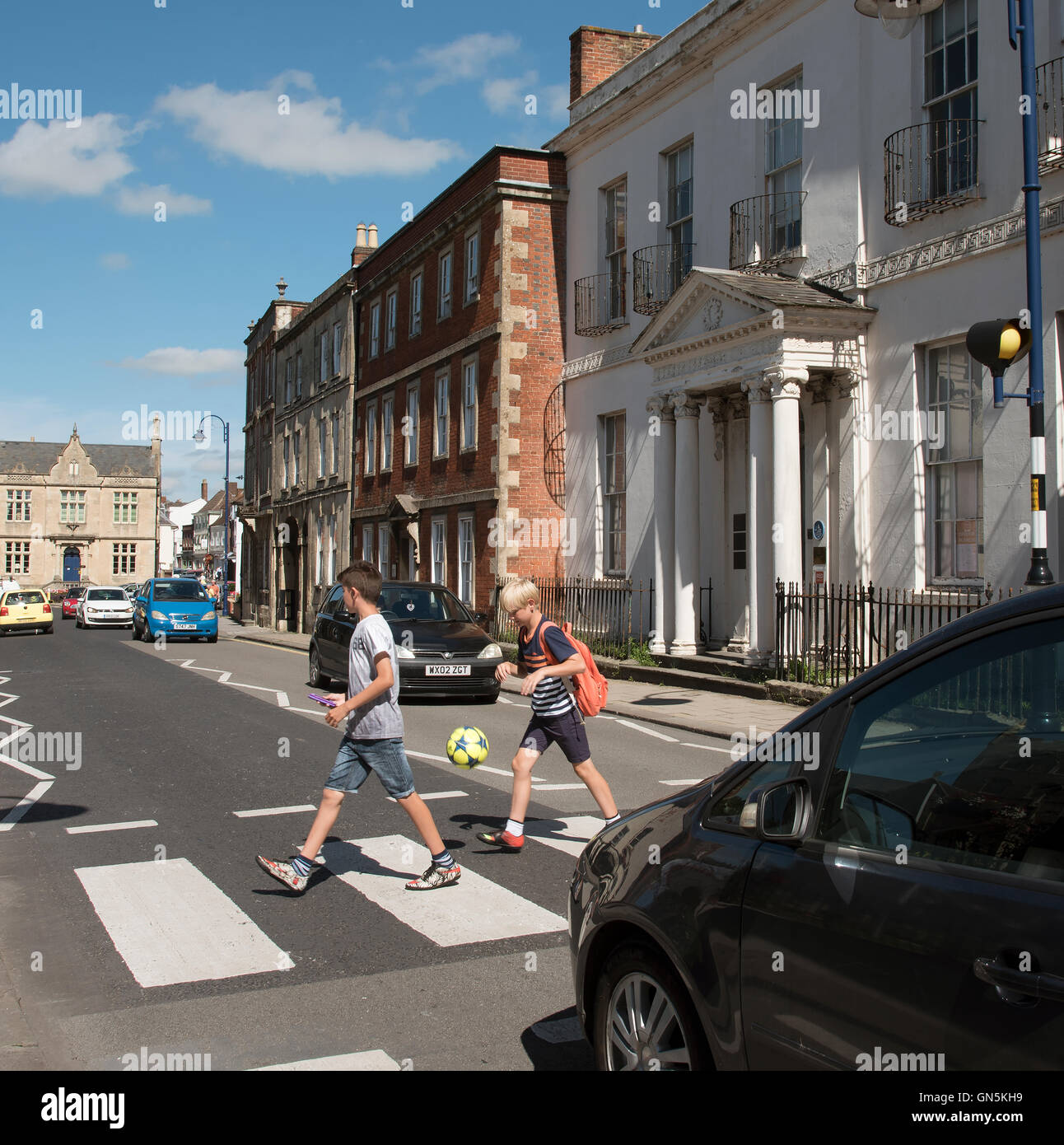 Young boys crossing the road on a panda crossing playing ball and using ...